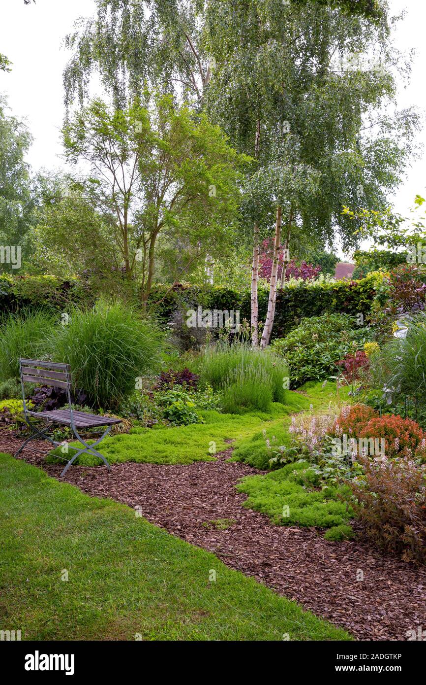 A bark path leading through woodland style herbaceous borders ...
