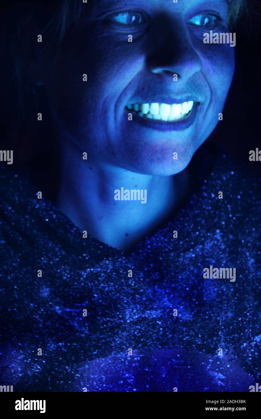 Woman's face in ultraviolet light. Her teeth are fluorescing, as are ...