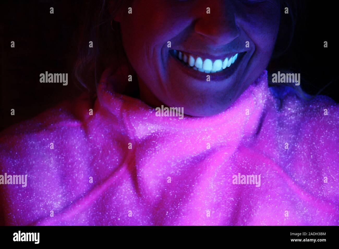 Woman smiling in ultraviolet light. Her teeth are fluorescing, as are ...