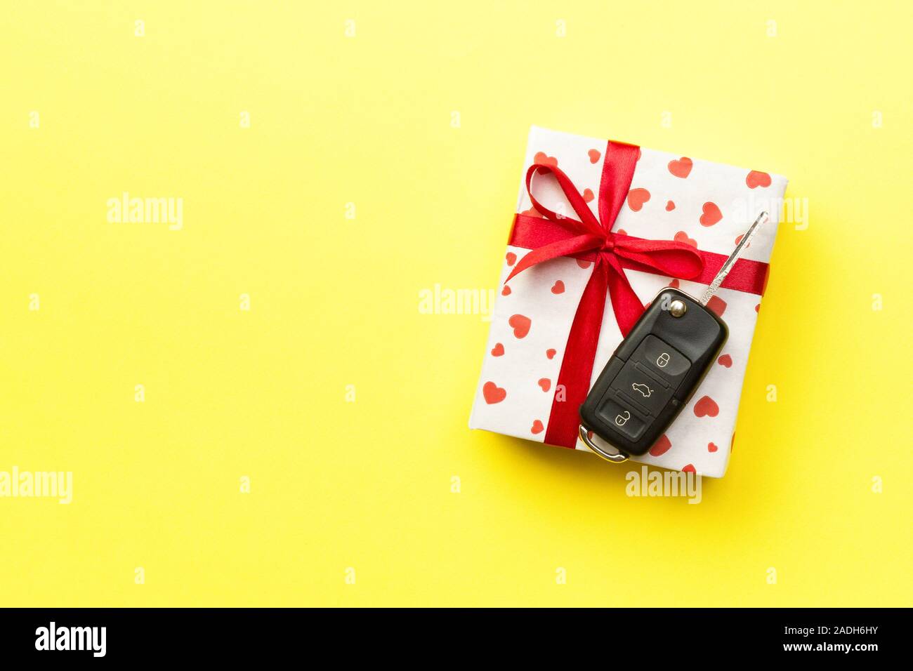 Car key on paper gift box with red ribbon bow and heart on yellow table ...