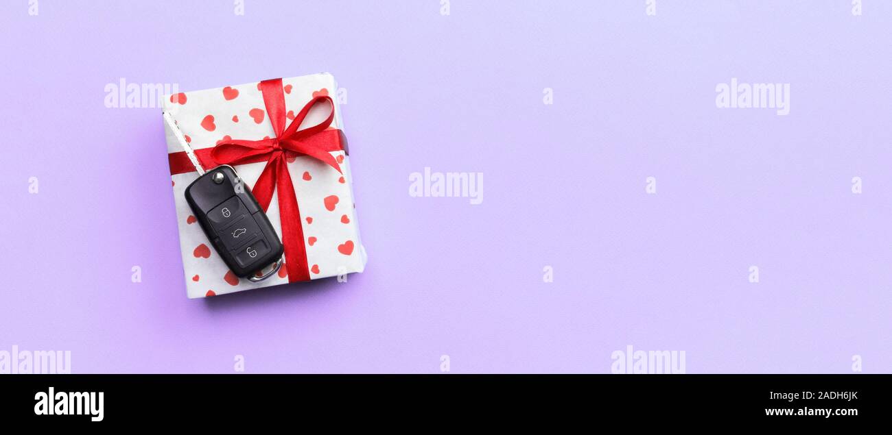 Car key on paper gift box with red ribbon bow and heart on violet table ...