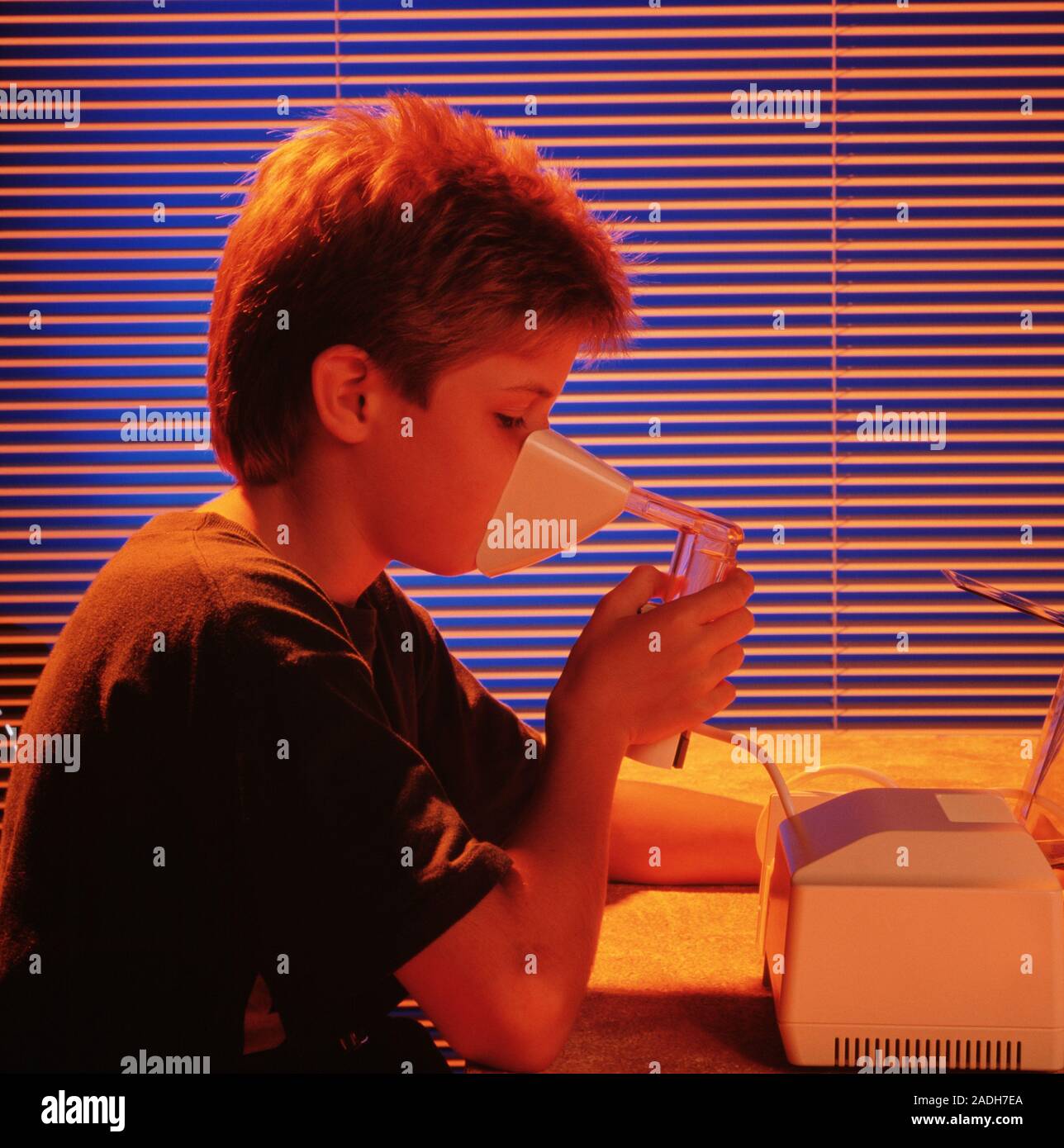 Asthma relief. Young boy breathes into the face-mask of a nebulizer, in ...