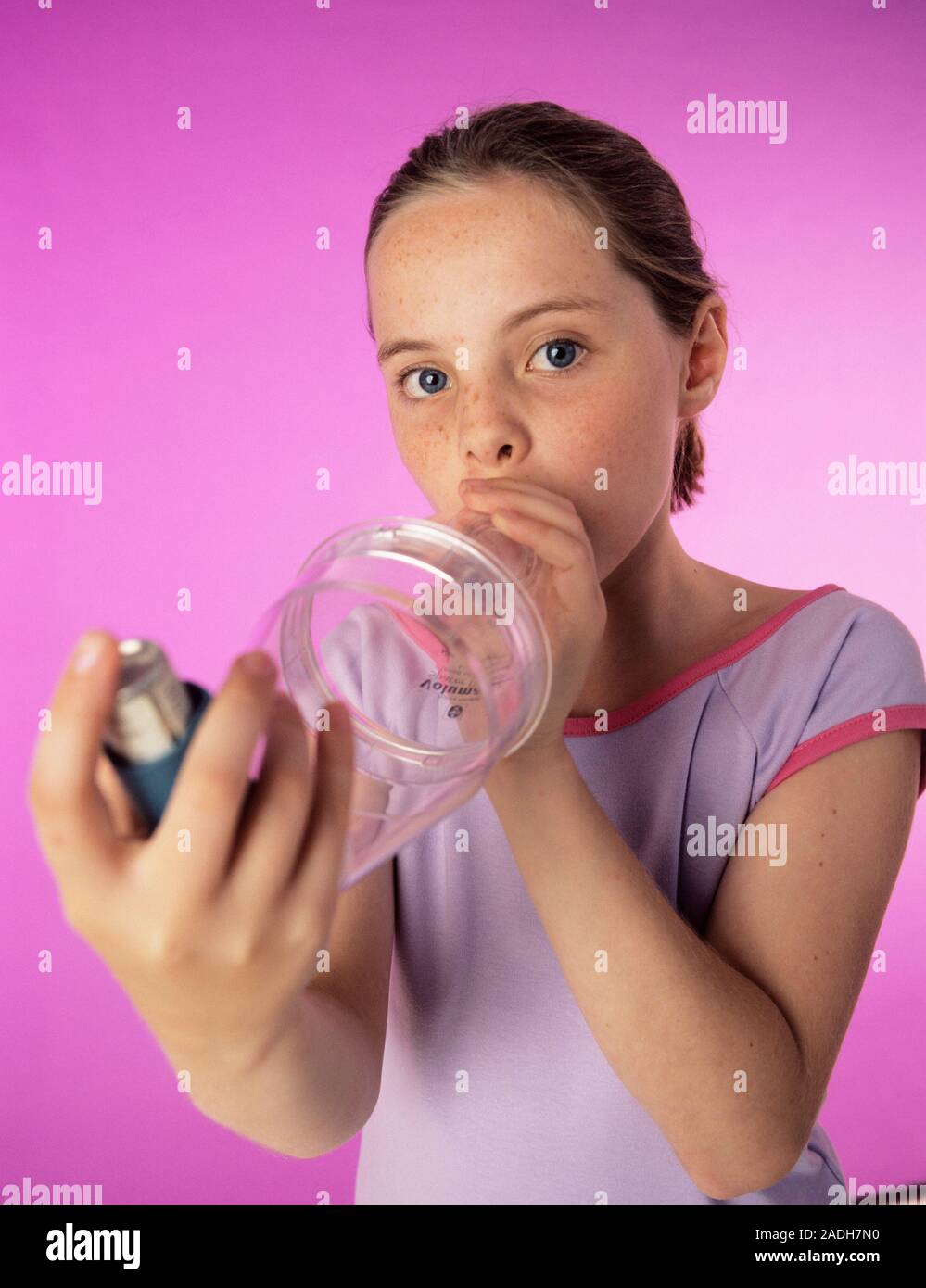 Asthma spacer. 8-year-old girl using a spacer (plastic chamber) with an ...