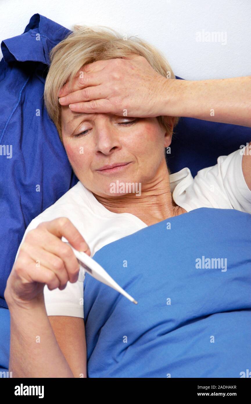 MODEL RELEASED. Woman suffering from a fever checking her temperature ...