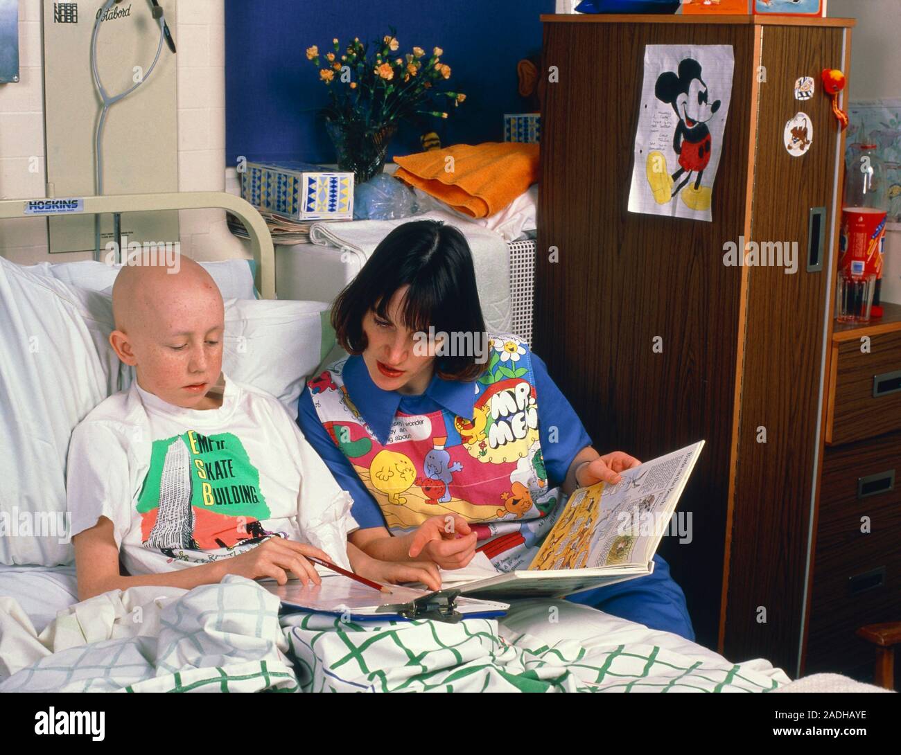 Paediatric nurse reading to a young boy with leukaemia. The boy is ...