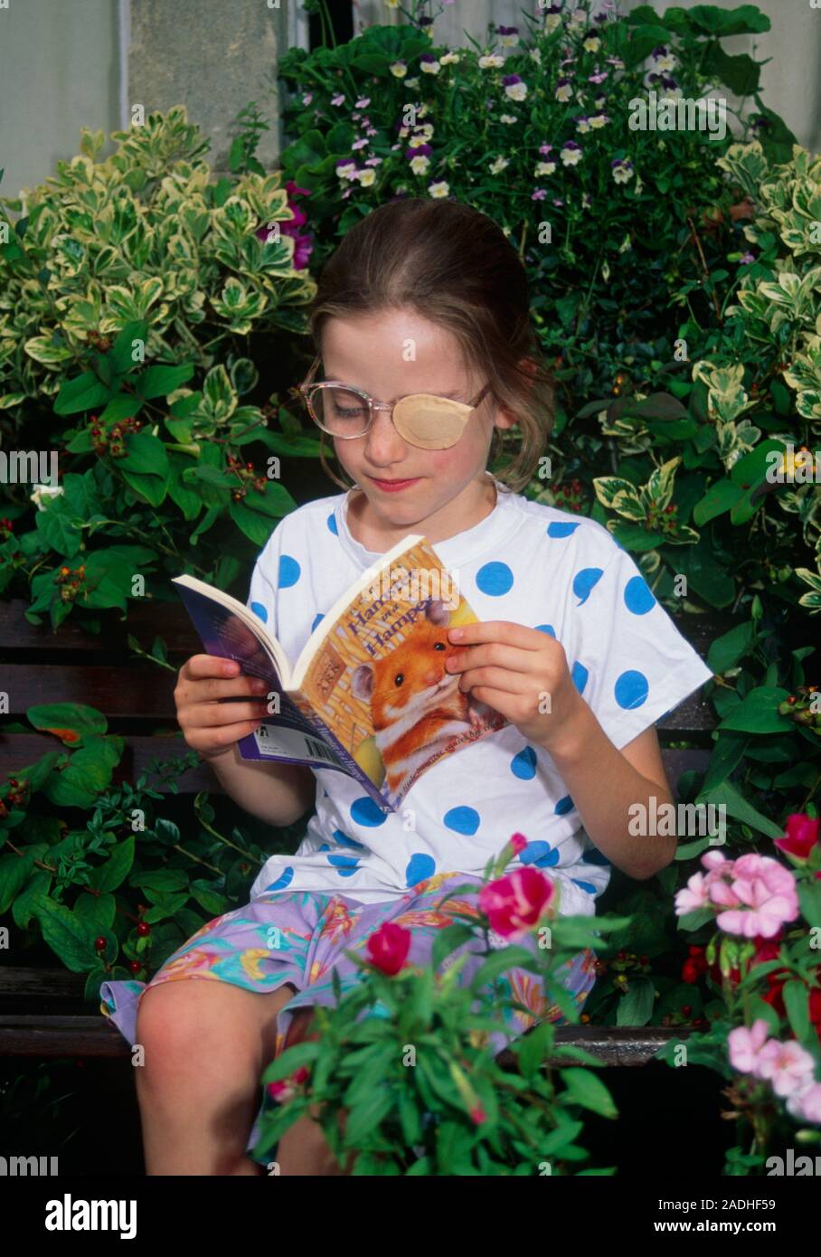 Lazy eye. Girl, aged 8, reads while wearing an eye patch over her left ...