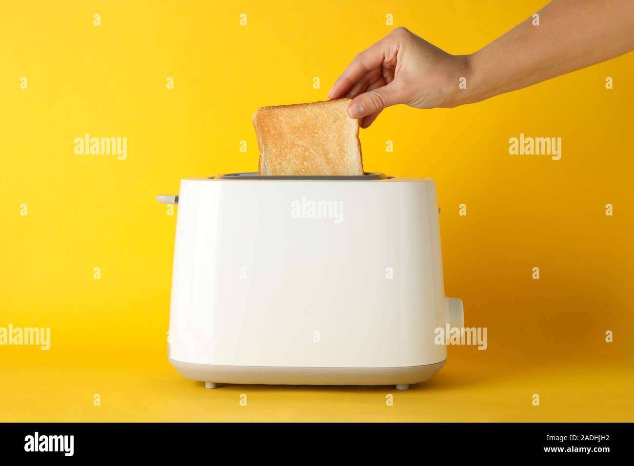 Female hand puts bread in a toaster on yellow background, space for ...