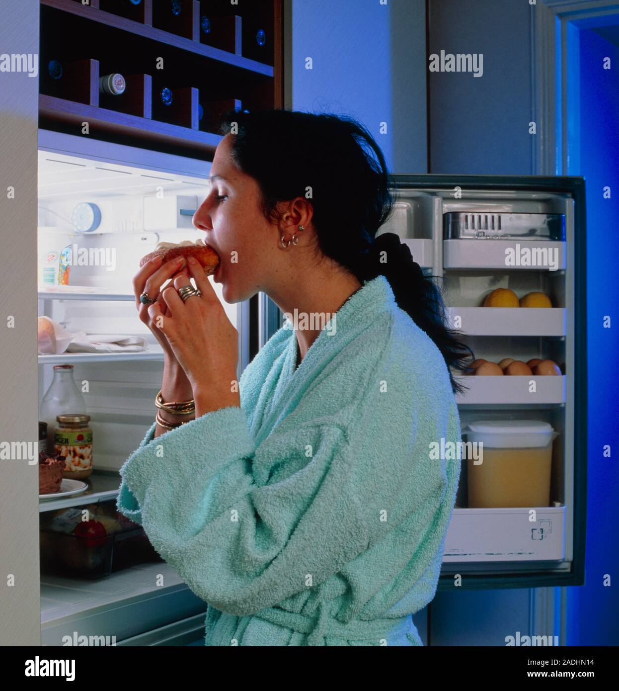 Female eating disorder. Young woman at a fridge craves food late at ...