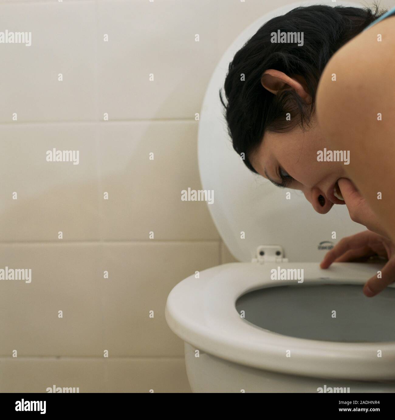 MODEL RELEASED. Bulimia. Young woman crouching over a toilet bowl with her fingers in her throat ...