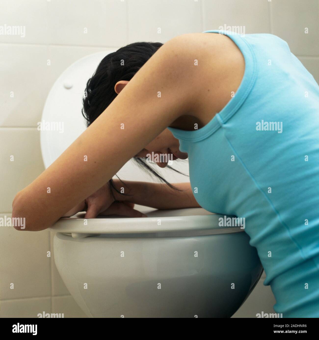 MODEL RELEASED. Bulimia. Young woman crouching over toilet bowl and self inducing vomiting ...