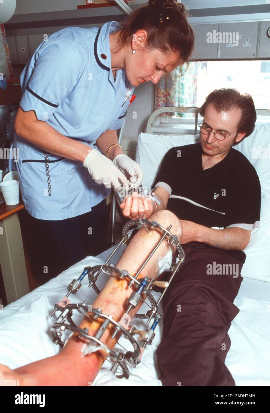 Broken leg. Nurse injecting antibiotics into a man's arm to treat a ...