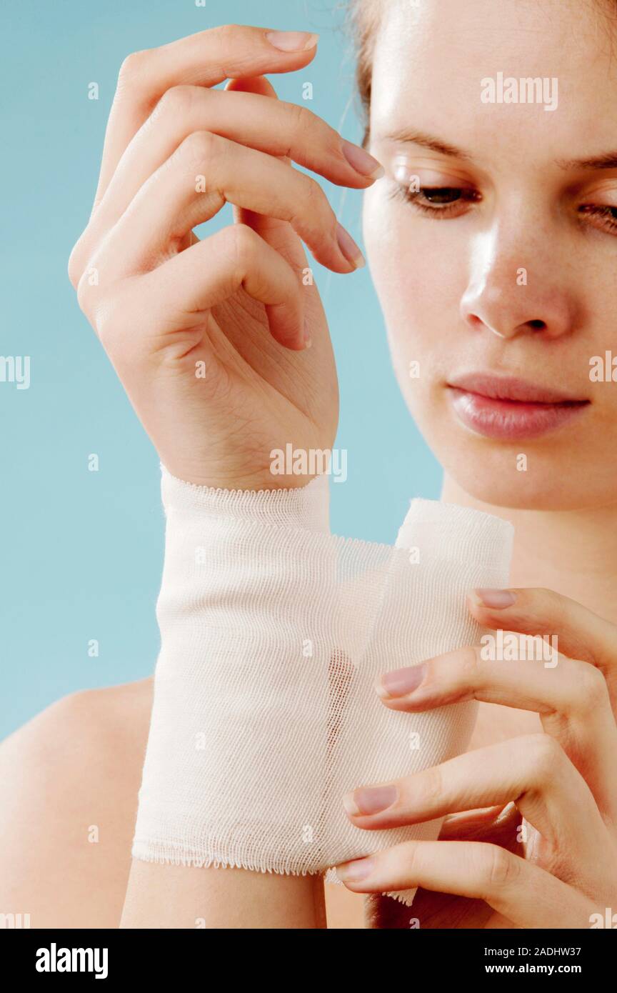 Sprained wrist. Woman wrapping a bandage around her wrist to immobilise ...