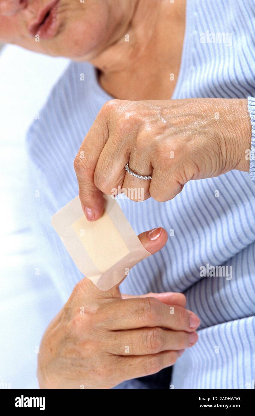 MODEL RELEASED. Cut finger. Elderly woman applying a sticking plaster ...