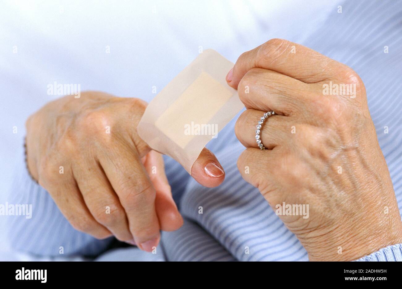 MODEL RELEASED. Cut finger. Elderly woman applying a sticking plaster ...