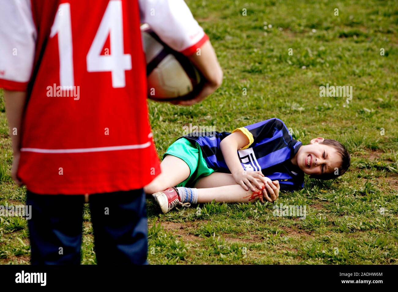 MODEL RELEASED. Knee injury. Boy lying on the ground holding his ...