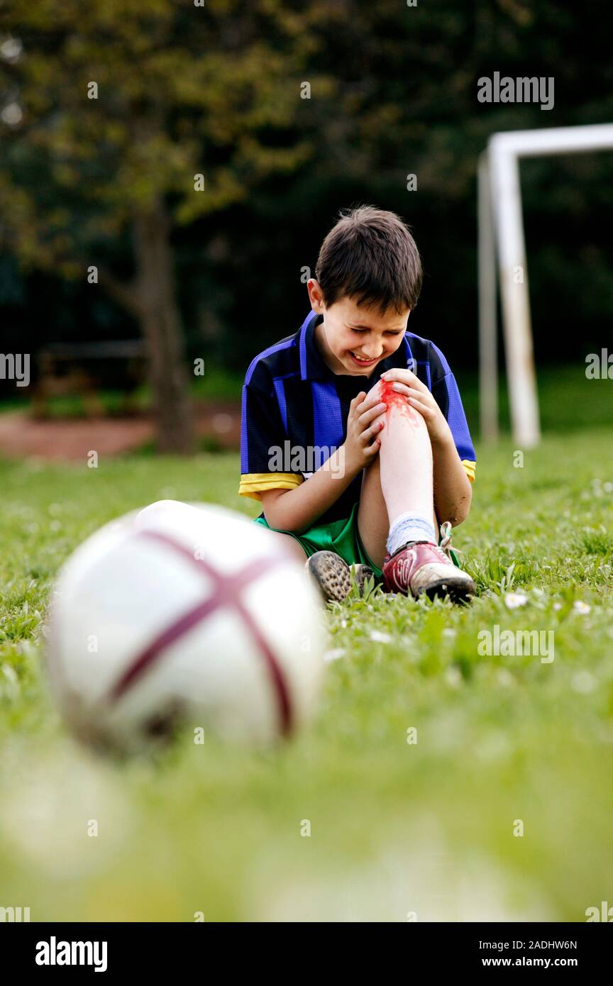 MODEL RELEASED. Knee injury. Boy holding his bleeding knee, which was ...