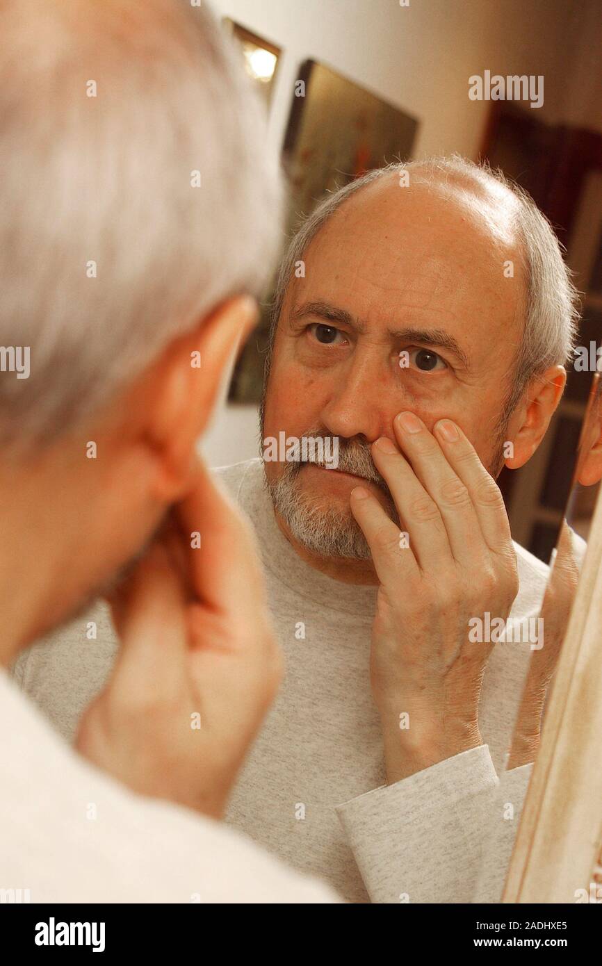 Signs of ageing. 65-year-old man looking in a mirror for signs of ...