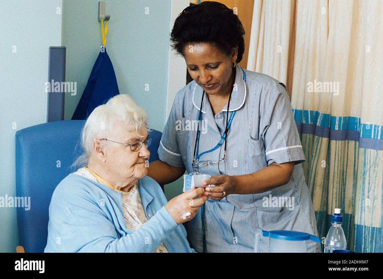 MODEL RELEASED. Geriatric care. Nurse passing medication to an elderly ...