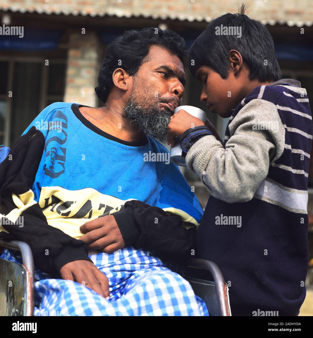 Disability. Boy helping a wheelchair user to take a drink. This man has ...