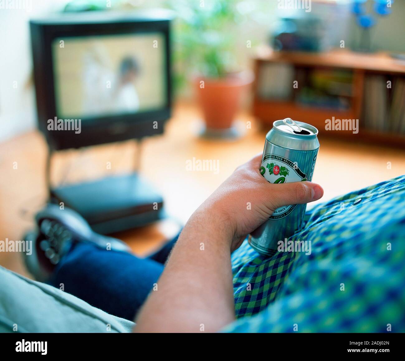 Beer can. Man holding a beer can as he sits on a couch and watches ...