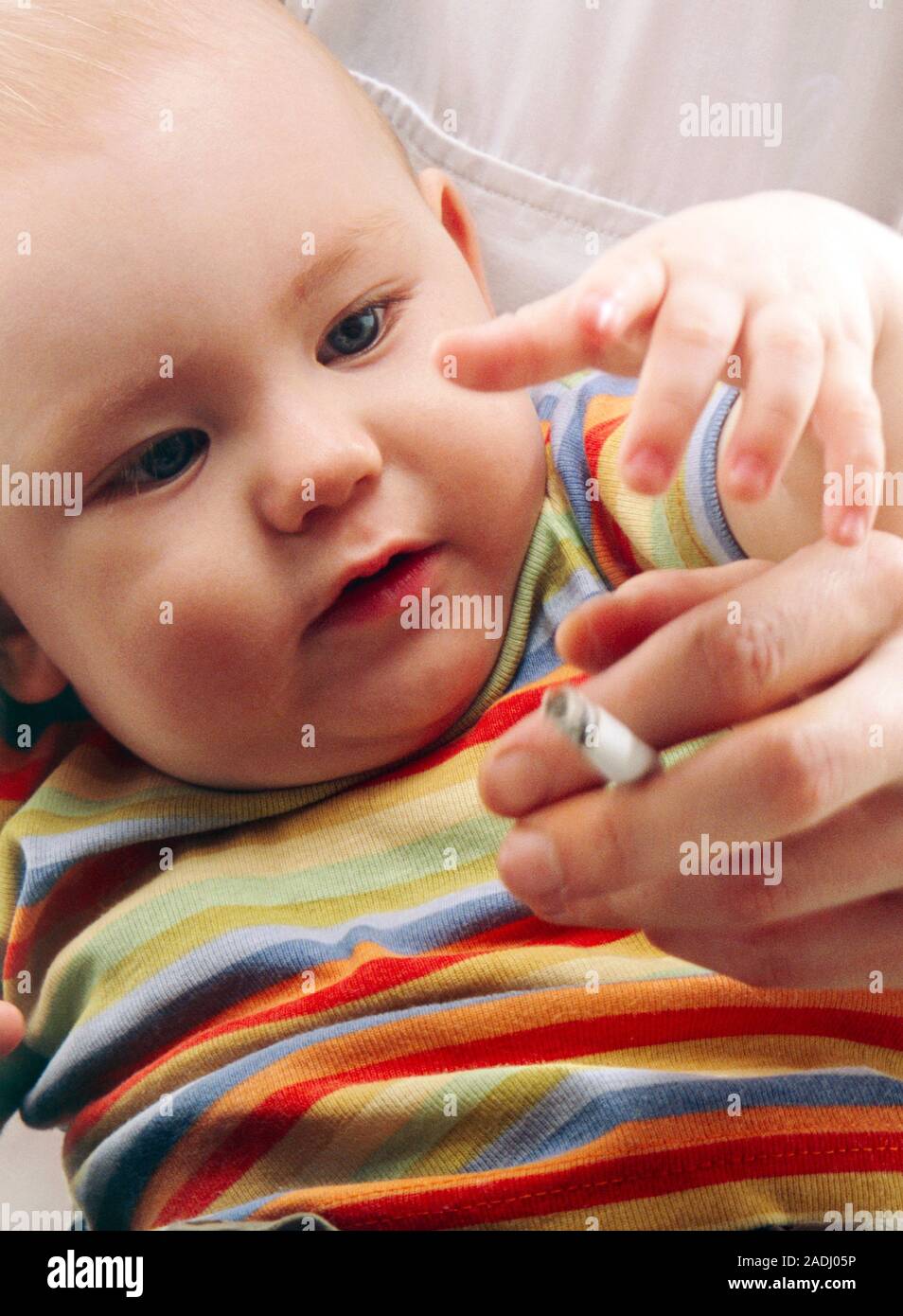MODEL RELEASED. Passive smoking. Baby reaching for a lit cigarette ...