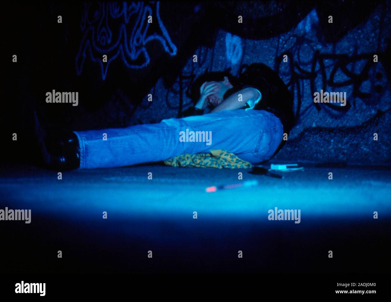Heroin addict. A heroin addict lies under a graffiti-covered wall next ...
