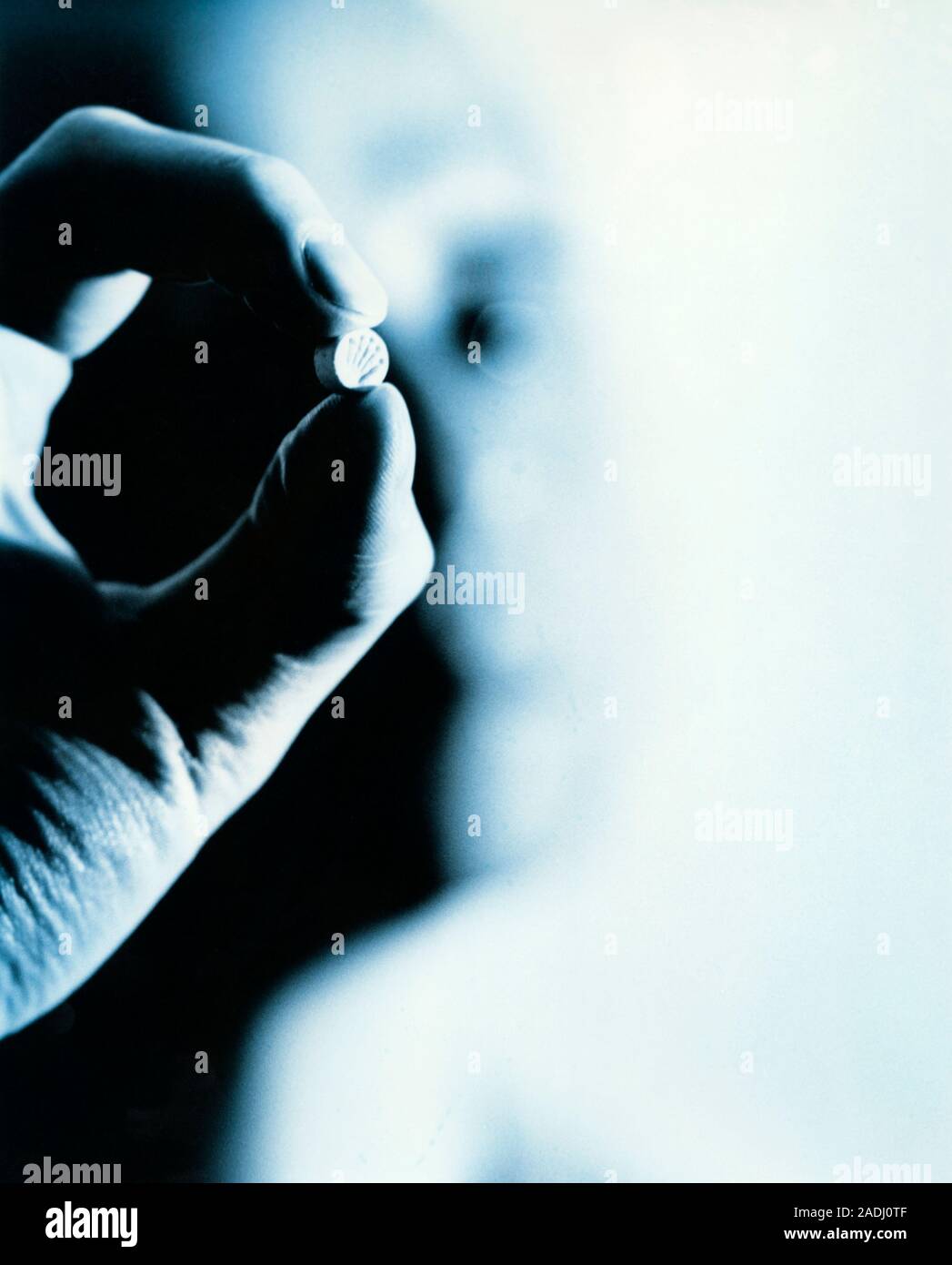 Ecstasy tablet. Fingers holding an ecstasy tablet imprinted with a ...