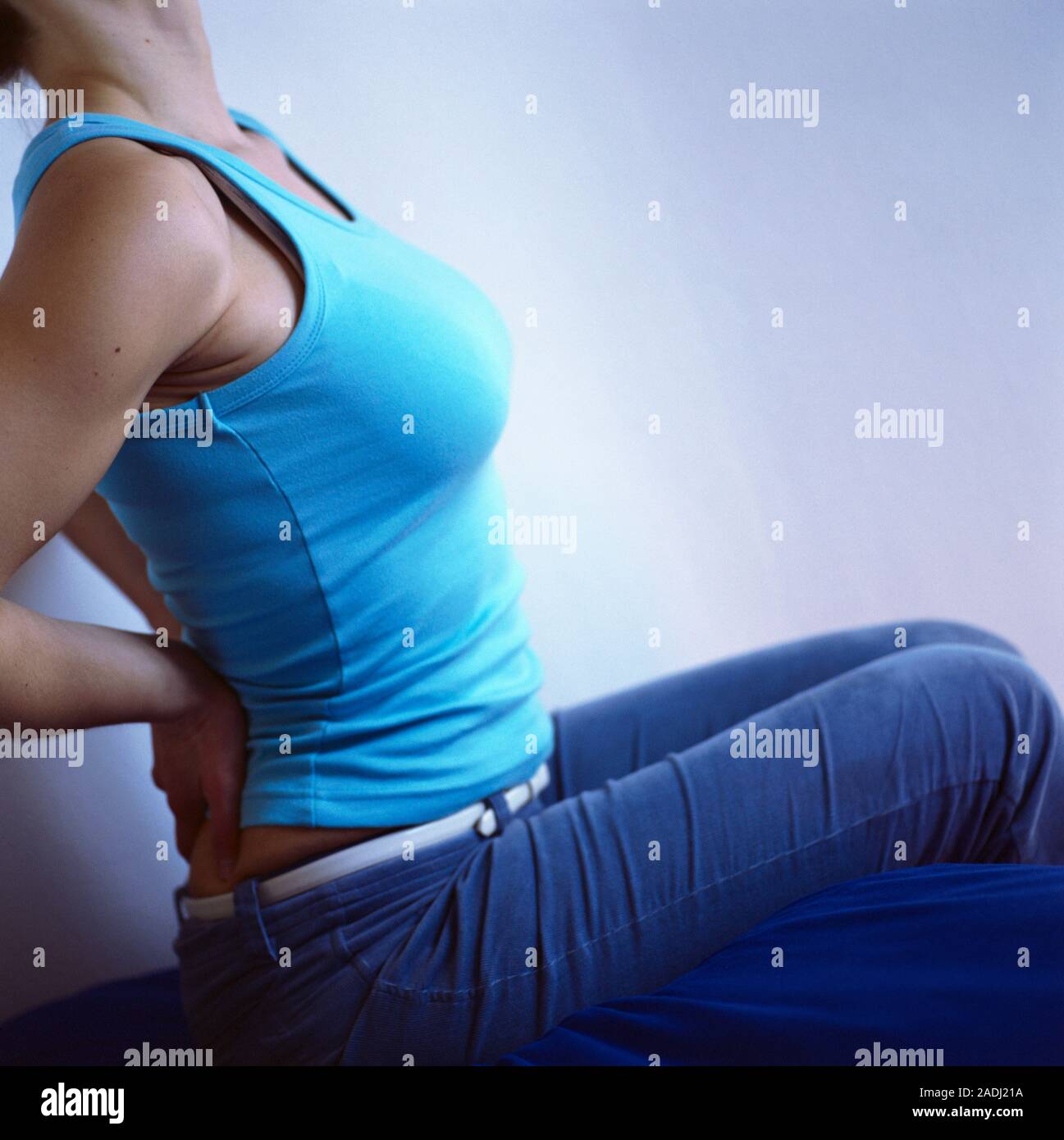 MODEL RELEASED. Lower back pain. Young woman holds her painful lower ...