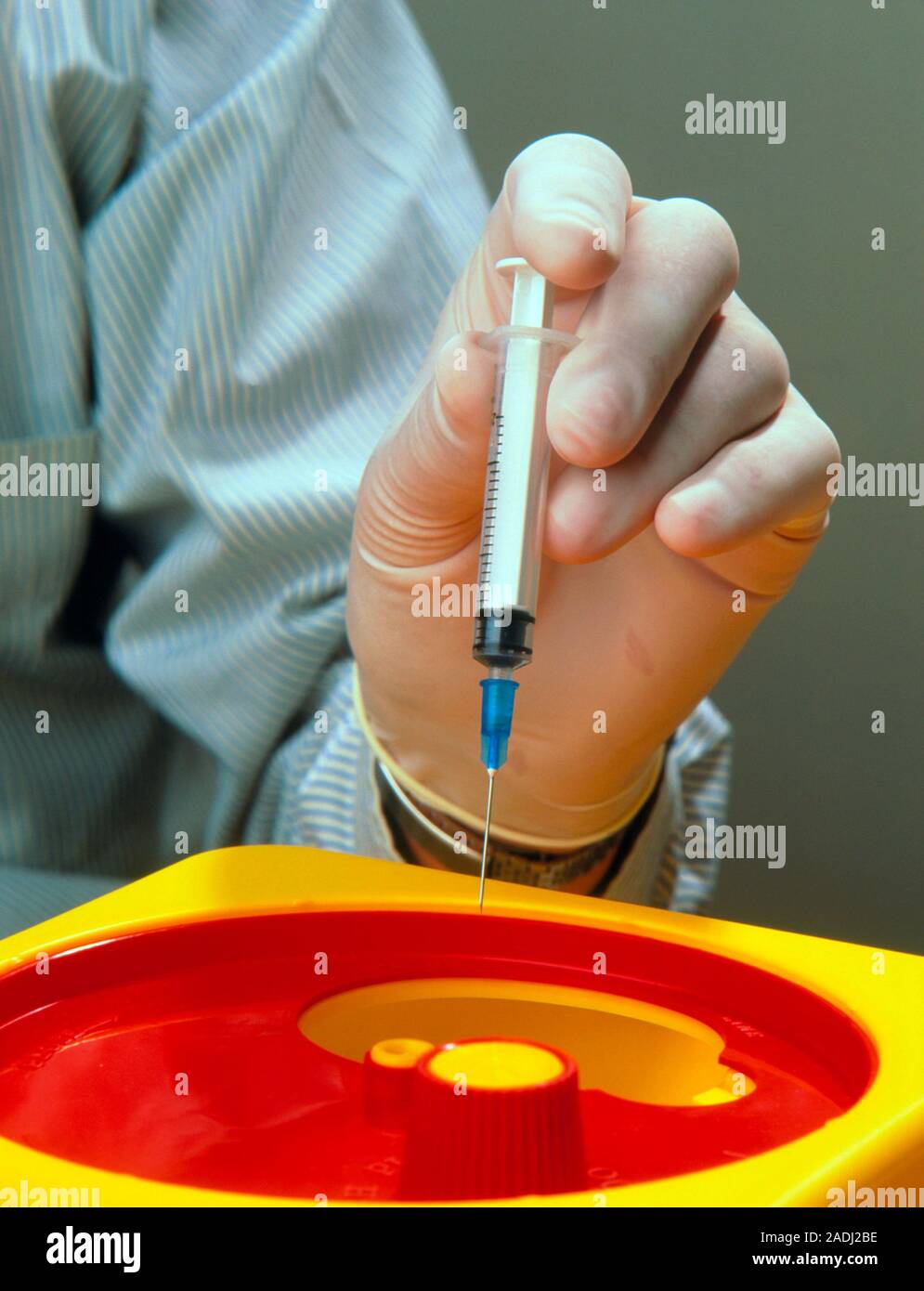 Syringe disposal. Close-up of a hypodermic syringe being dropped into a ...