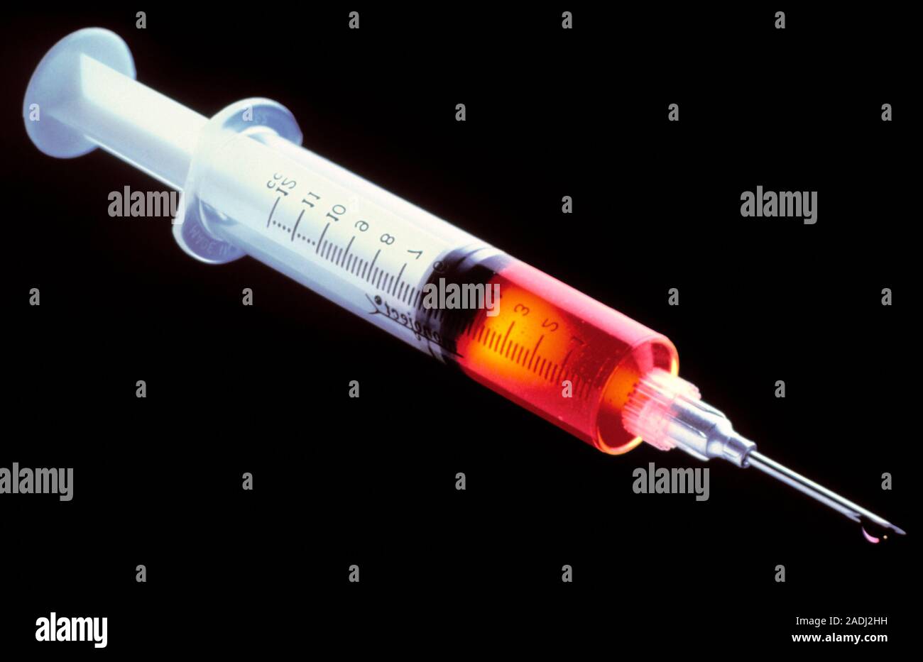 Syringe. View of a syringe filled with red liquid with a drop hanging ...