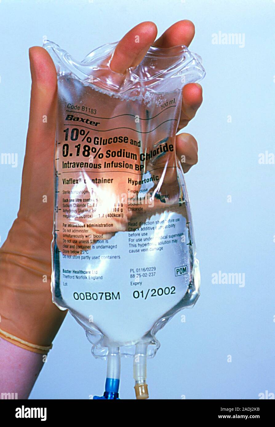 Intravenous drip. Gloved hand holding a glucose and saline drip. This ...