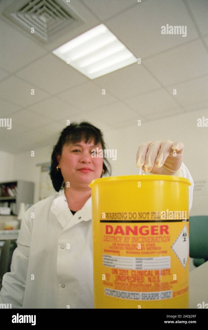 Sharps bin. Technician disposing of a contaminated item in a sharps bin ...