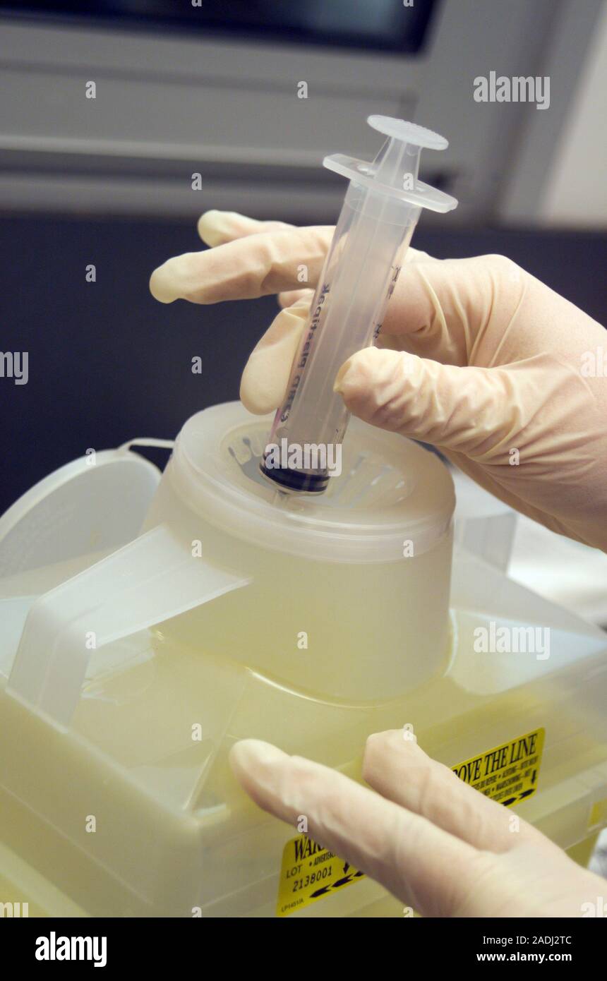 Medical waste disposal. Gloved hands of a nurse placing a used syringe ...