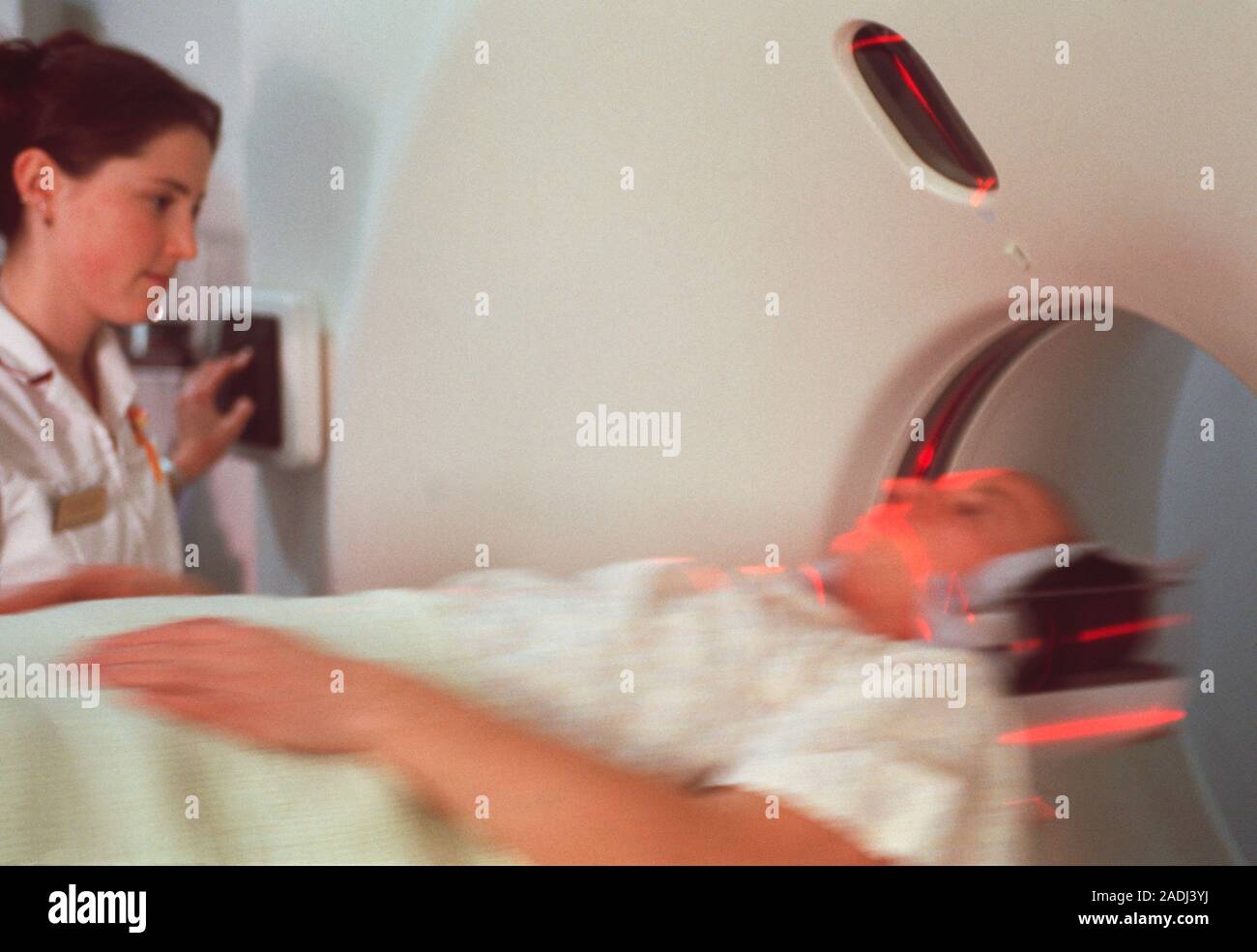 CT scanning. Radiologist preparing a male patient for a head scan in a ...