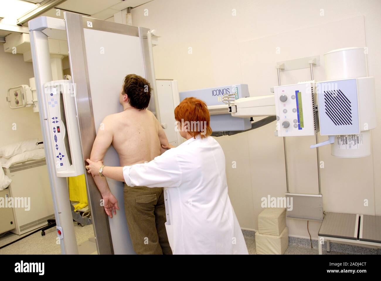 MODEL RELEASED. Chest X-ray. Radiographer positioning a patient in front of an X-ray machine ...