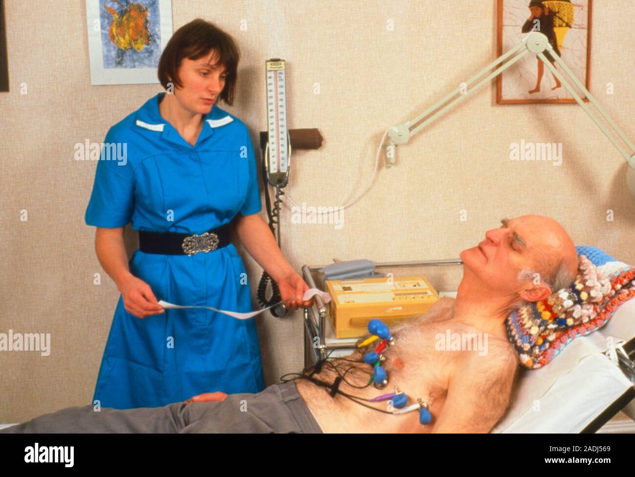A nurse monitors the heartbeat of an elderly man fitted with chest ...
