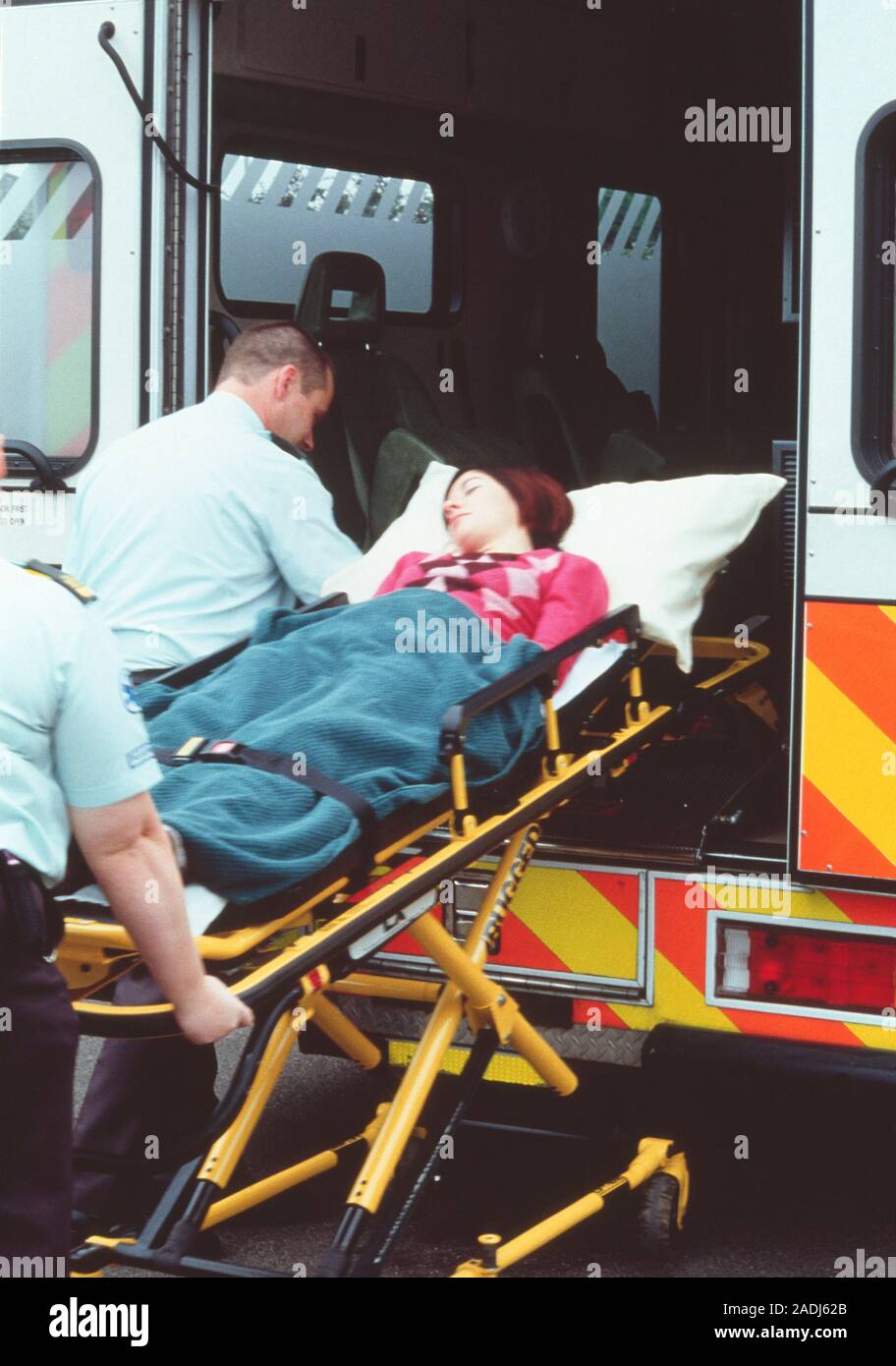 Ambulance treatment. Paramedics moving a patient on a trolley into an ...