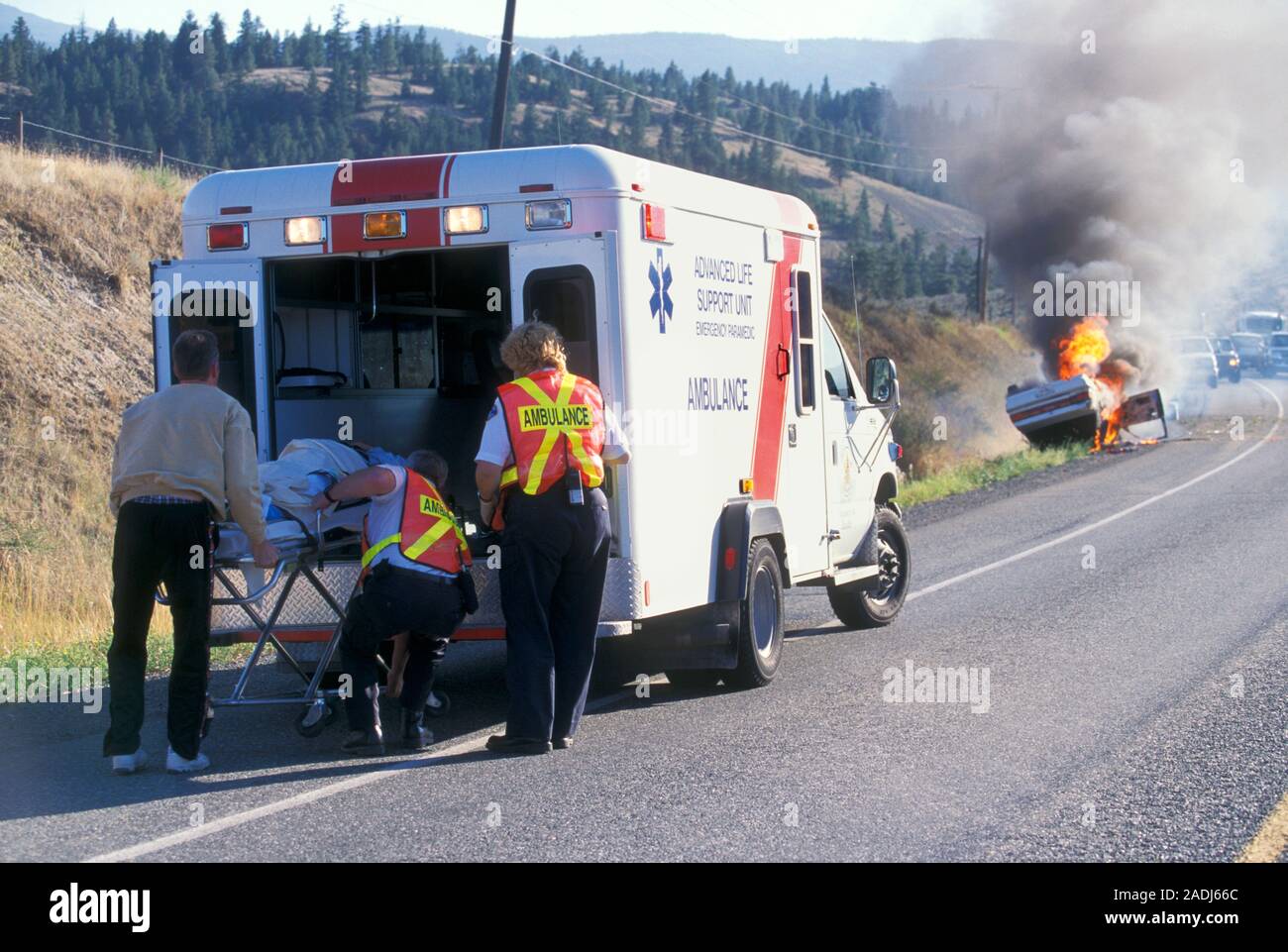 Road accident. Member of the public helping paramedics load a patient ...
