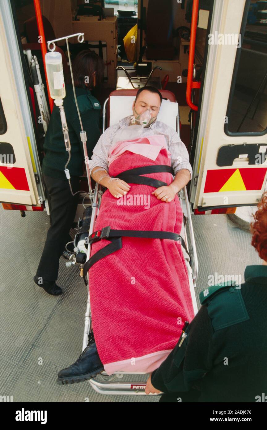 Emergency treatment. Ambulance crew moving a male patient out of an ...