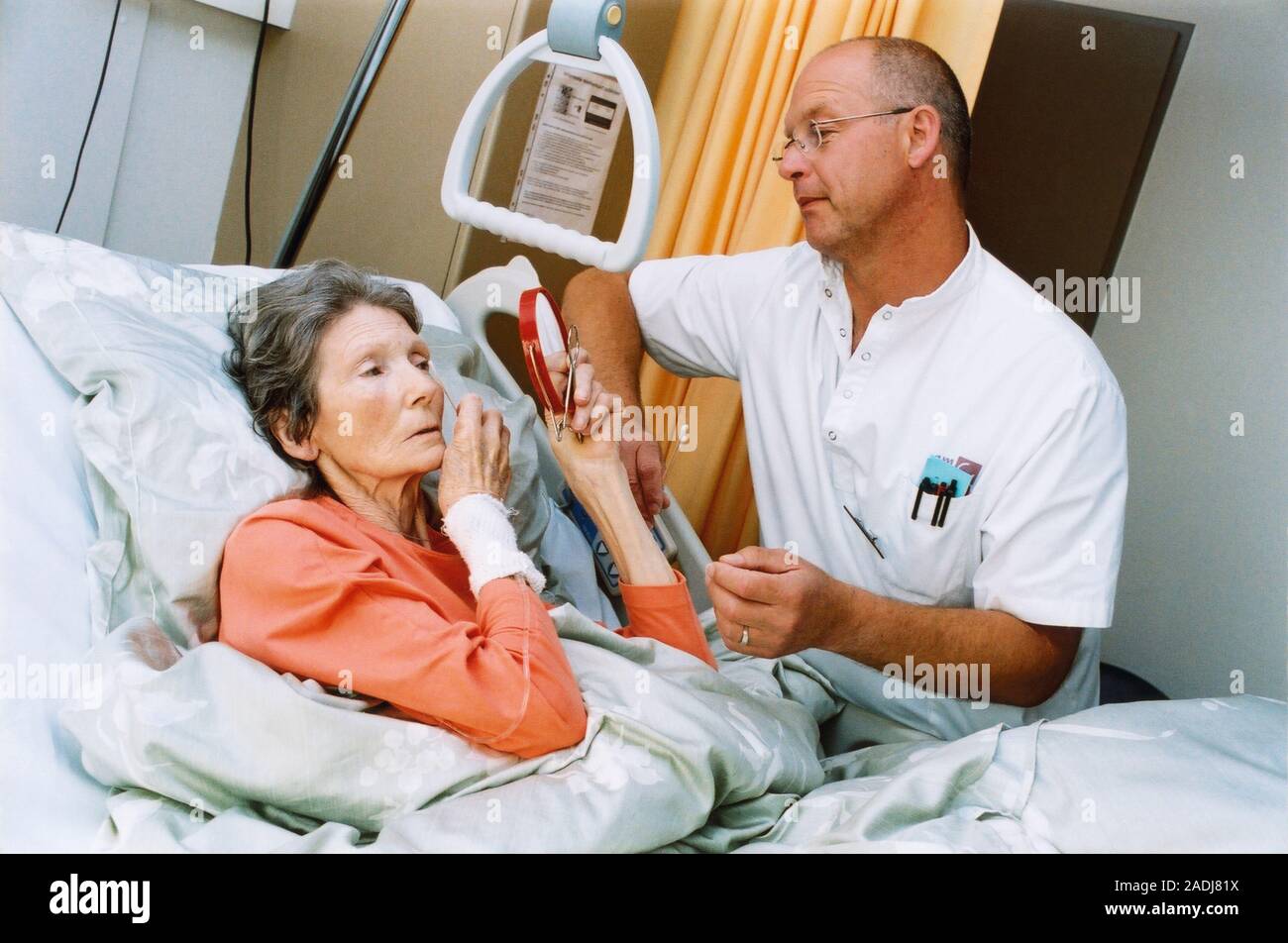 Terminal care. Hospital nurse helping a terminally ill patient to apply ...