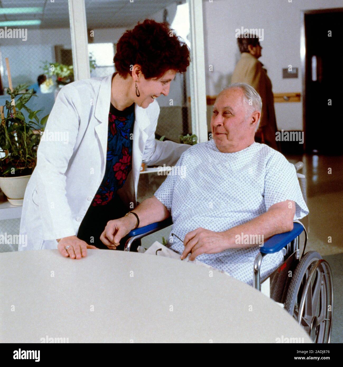 Geriatric ward. Nurse attending to an elderly man in a wheelchair in ...
