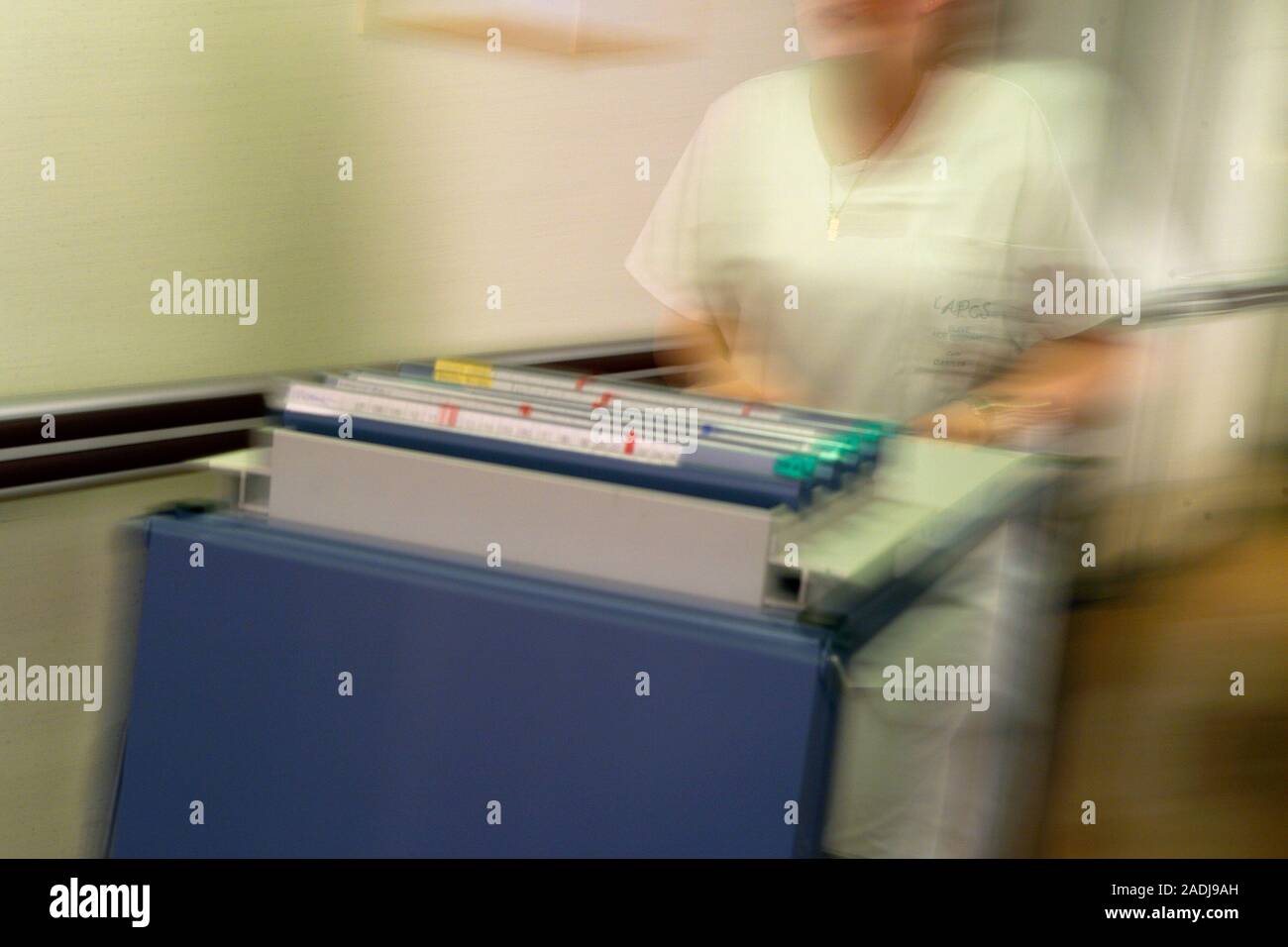 Medical records. Nurse pushing a filing cabinet of patients' records ...