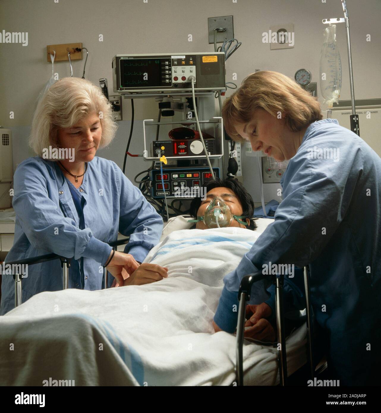 Recovery room. Two female nurses monitor an unconscious, anaesthetised ...