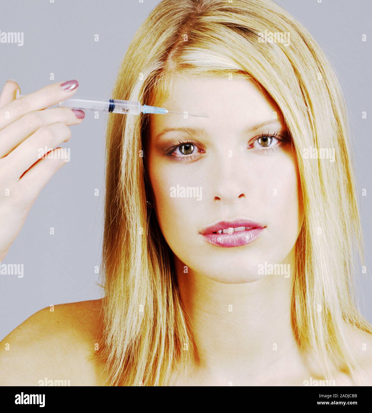 Woman using botox. Woman holding a syringe of botox to her forehead ...