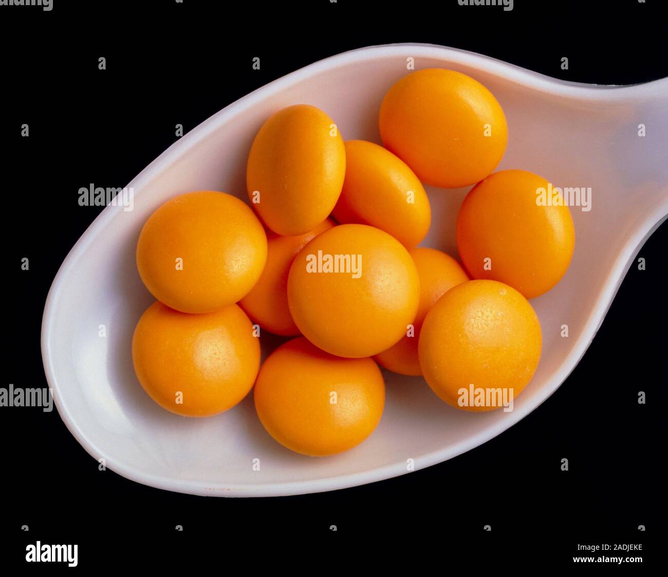 Vitamins. Group of orange multivitamin pills on a white plastic spoon ...