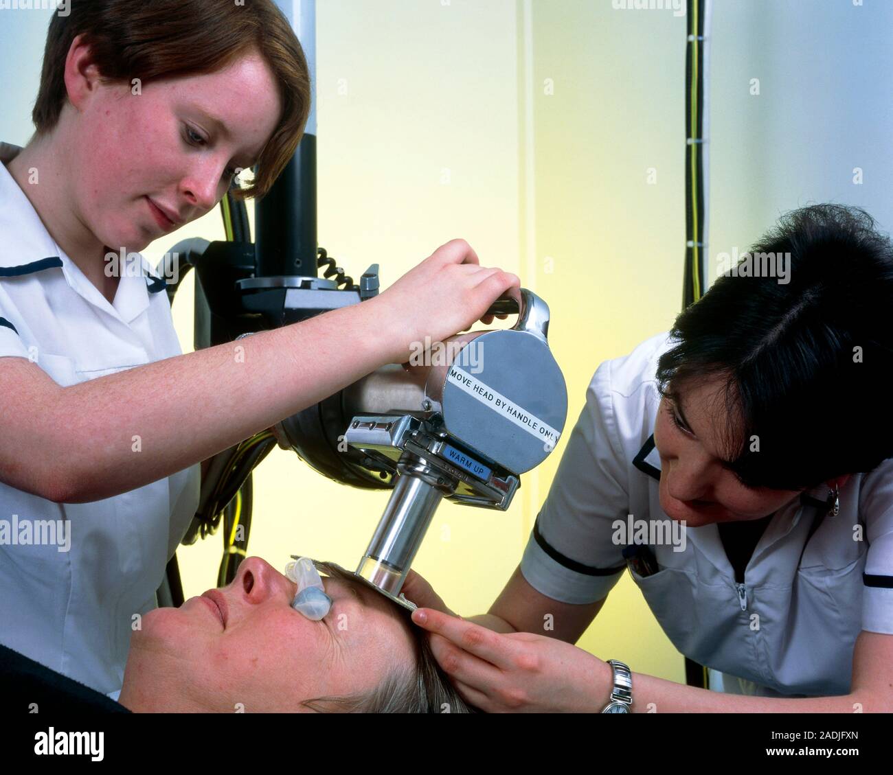 Radiotherapy. Radiographers position an X-ray generator over a woman's ...