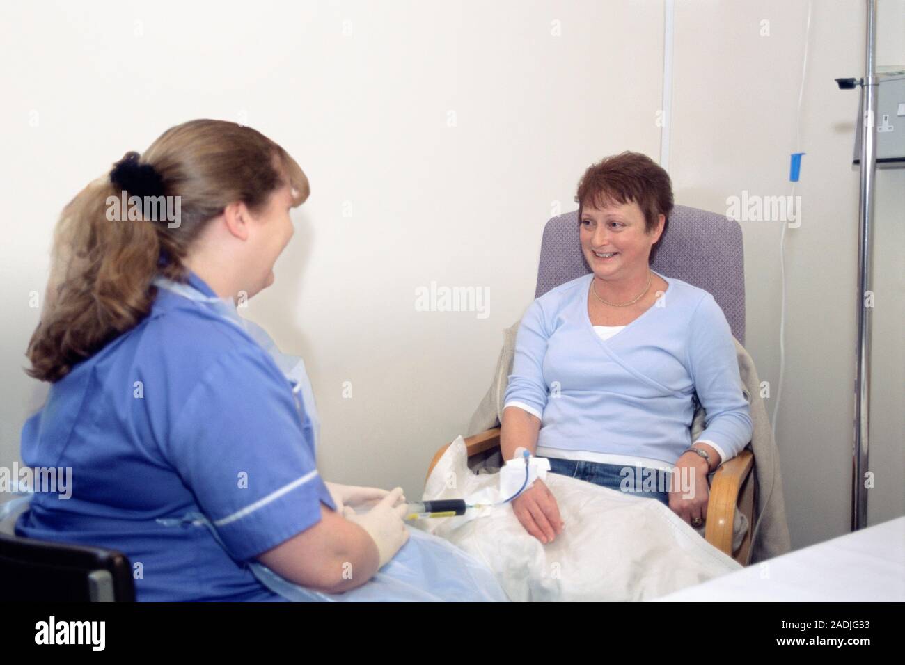 Cancer chemotherapy. Hospital nurse using a syringe (lower centre) to ...