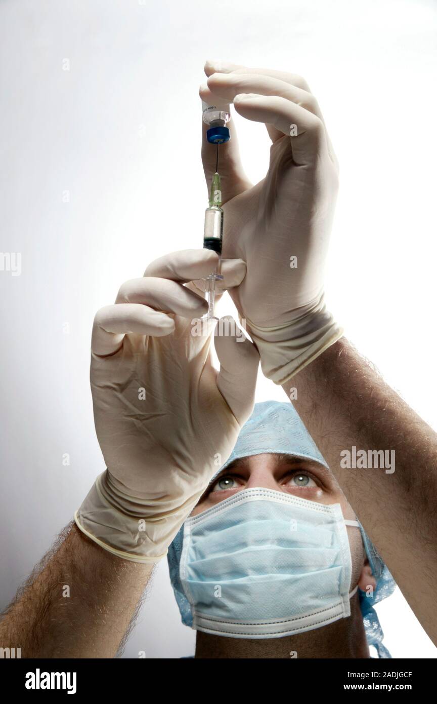 Preparing an injection. Doctor in sterile clothing drawing a drug into ...