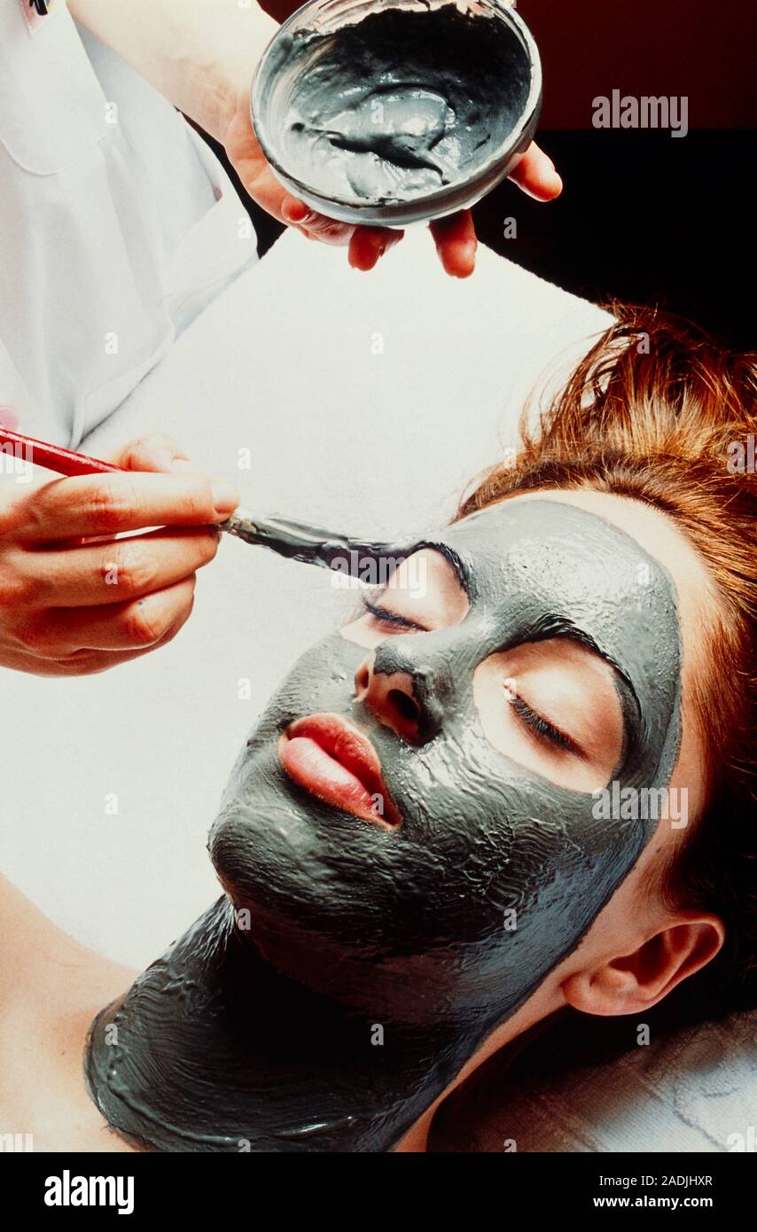 Mud pack. Hand applying mud to a woman's face with a brush. Health ...