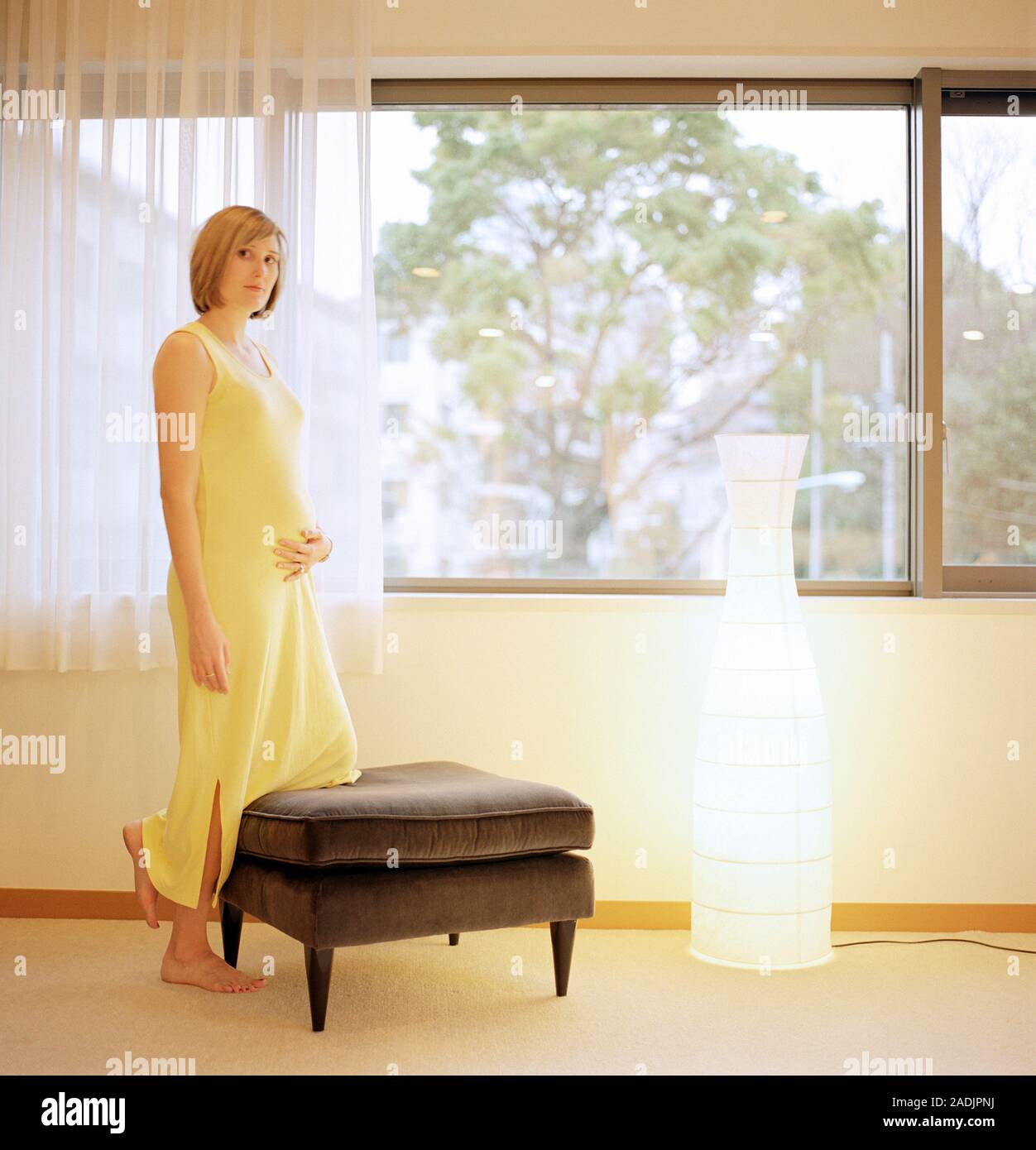 MODEL RELEASED. Pregnant woman standing beside a window and lamp. She ...